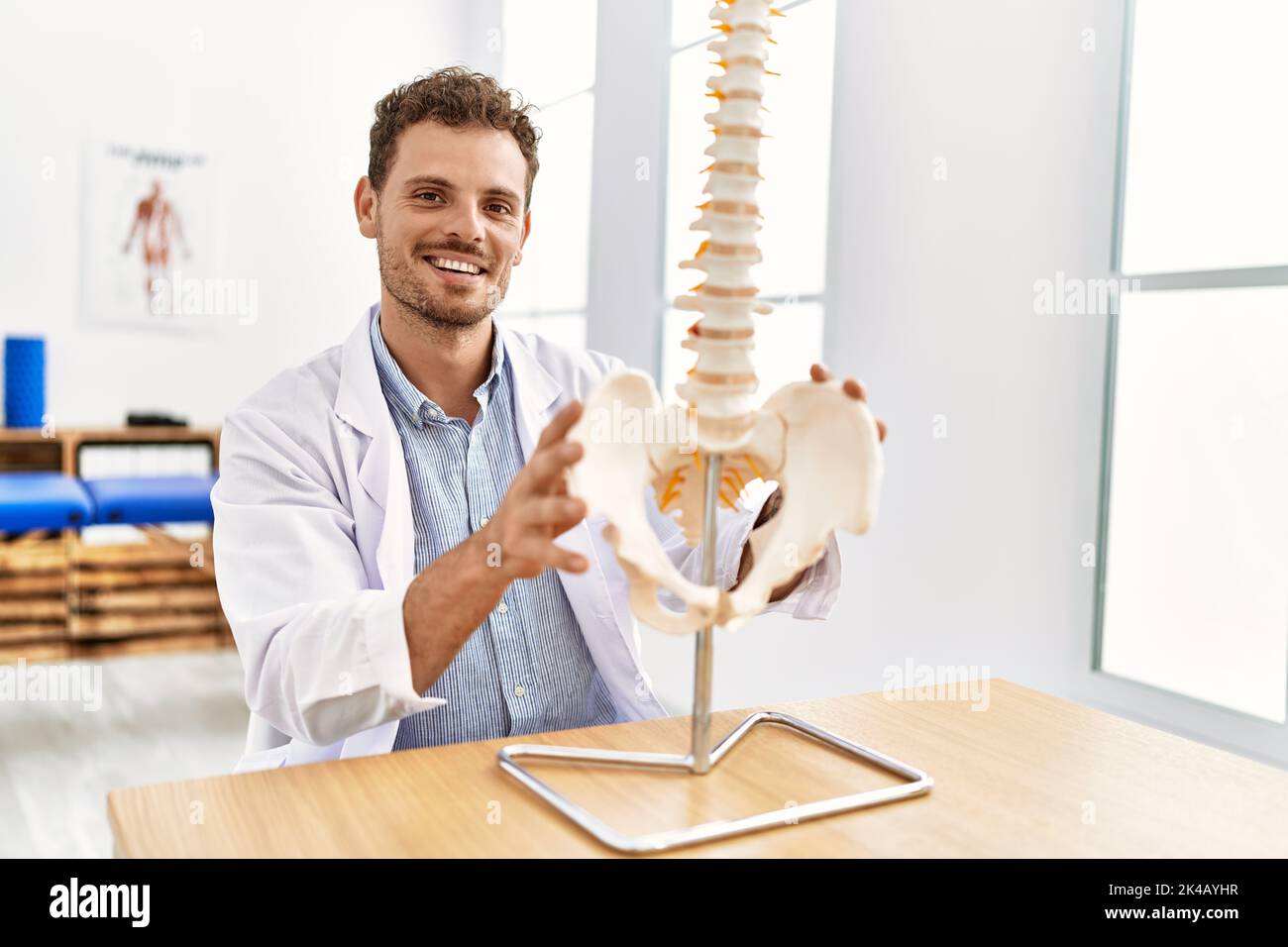 Young hispanic man wearing physiotherapist uniform touching anatomical ...