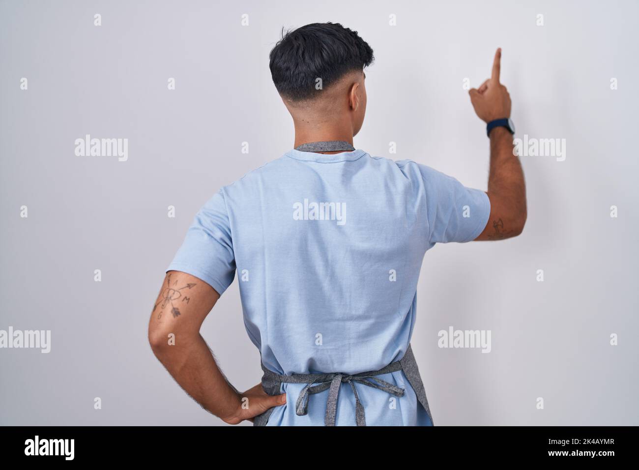 Hispanic young man wearing apron over white background posing backwards ...
