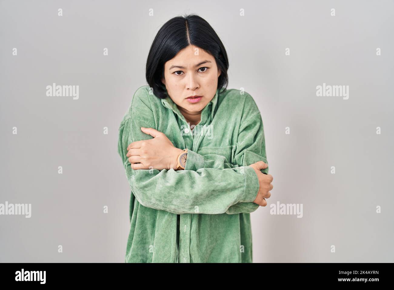 Young asian woman standing over white background shaking and freezing ...