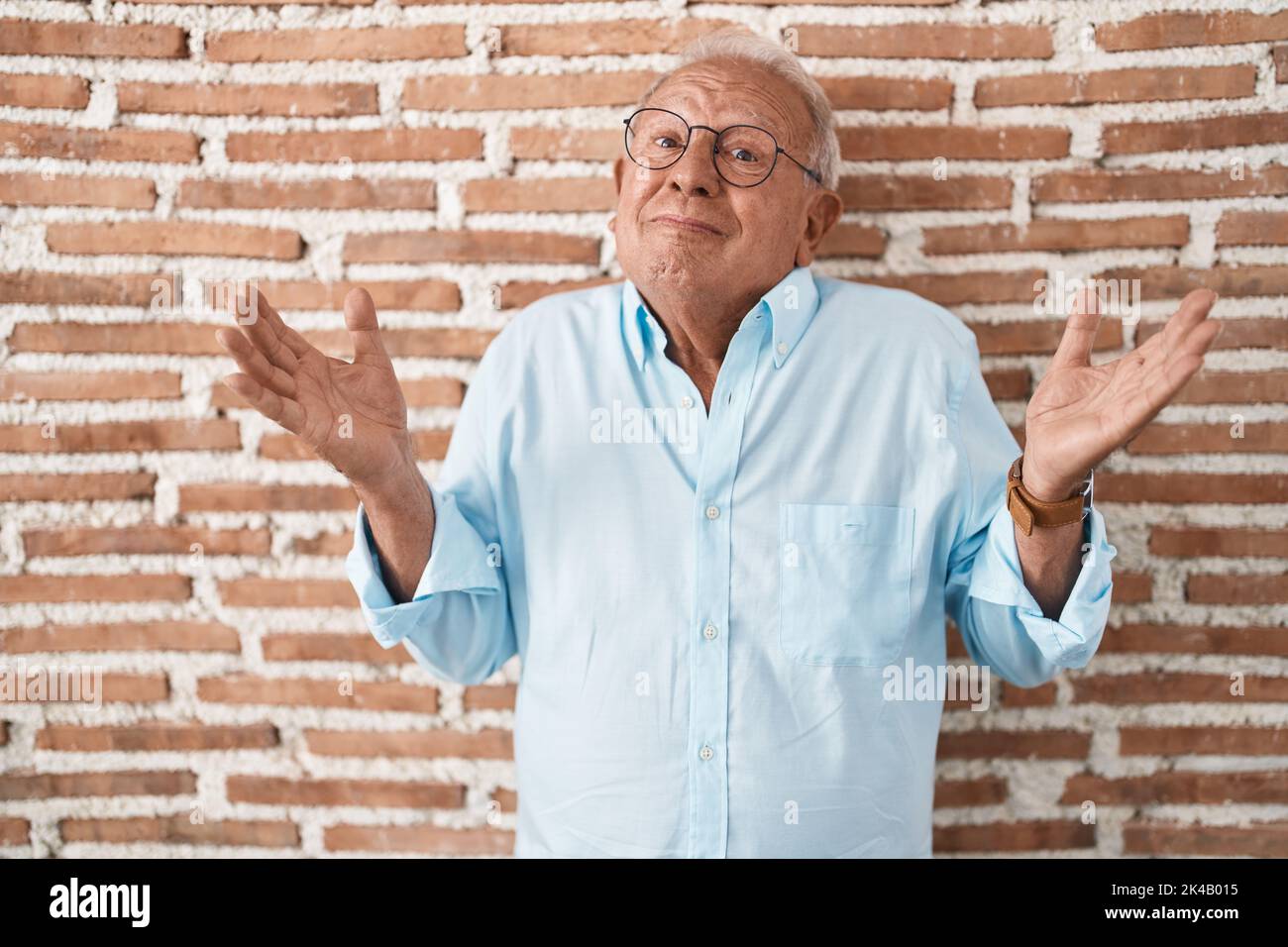 Senior man with grey hair standing over bricks wall clueless and ...