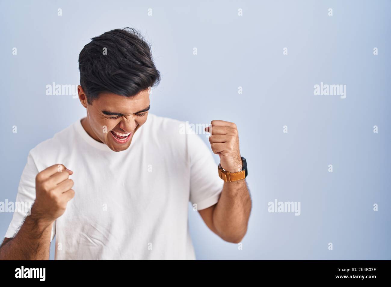 Hispanic man standing over blue background very happy and excited doing ...