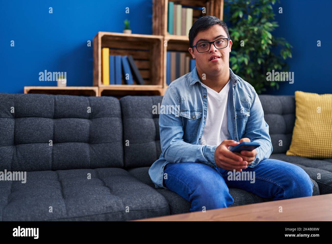 Down syndrome man using smartphone sitting on sofa at home Stock Photo ...