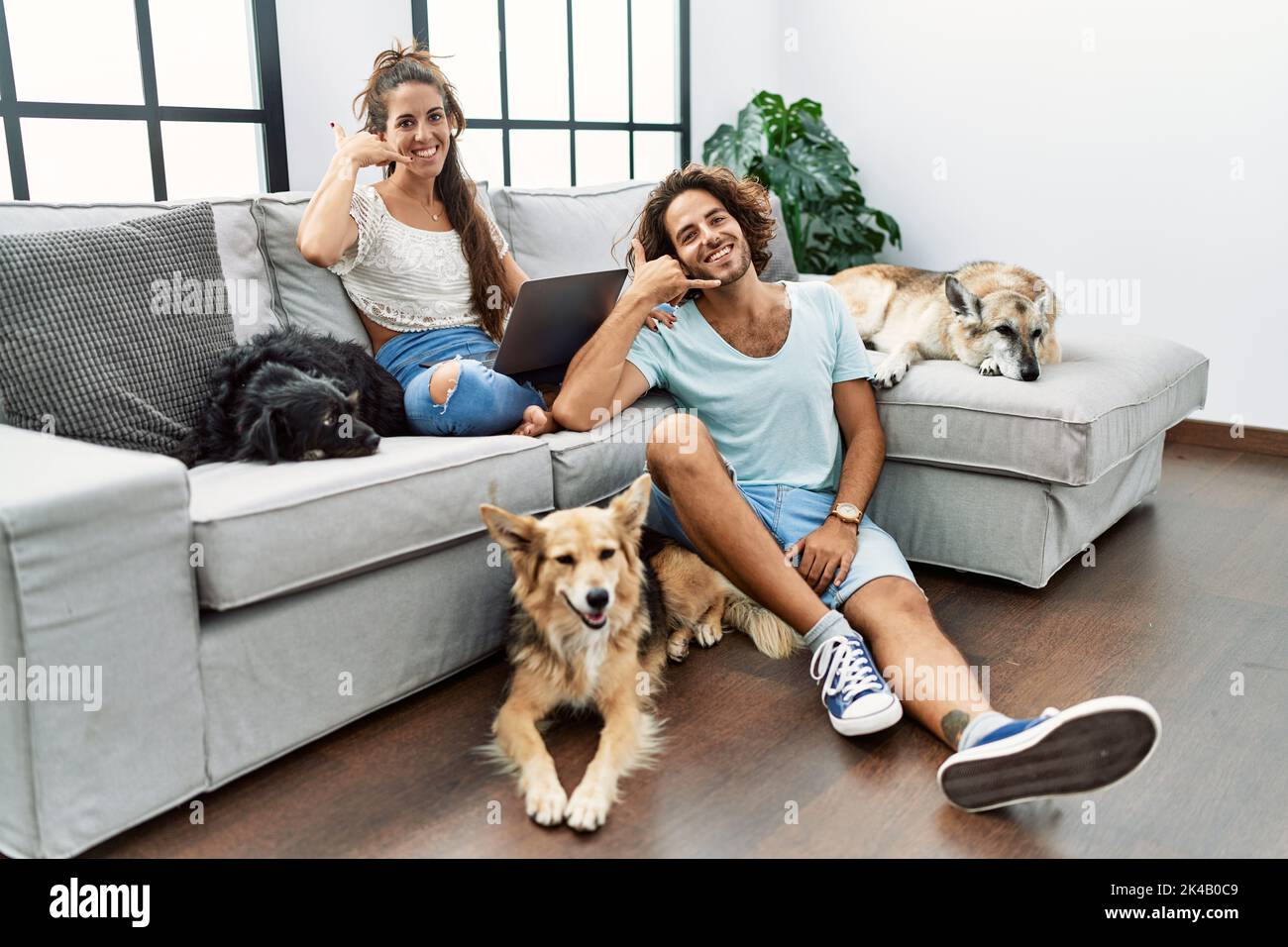 Young hispanic couple with dogs relaxing at home smiling doing phone ...
