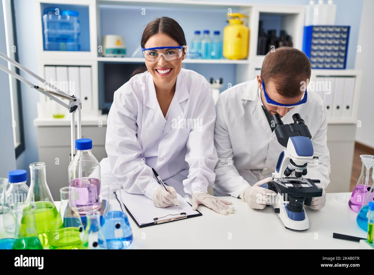 Man and woman scientist partners working using microscope and writing ...