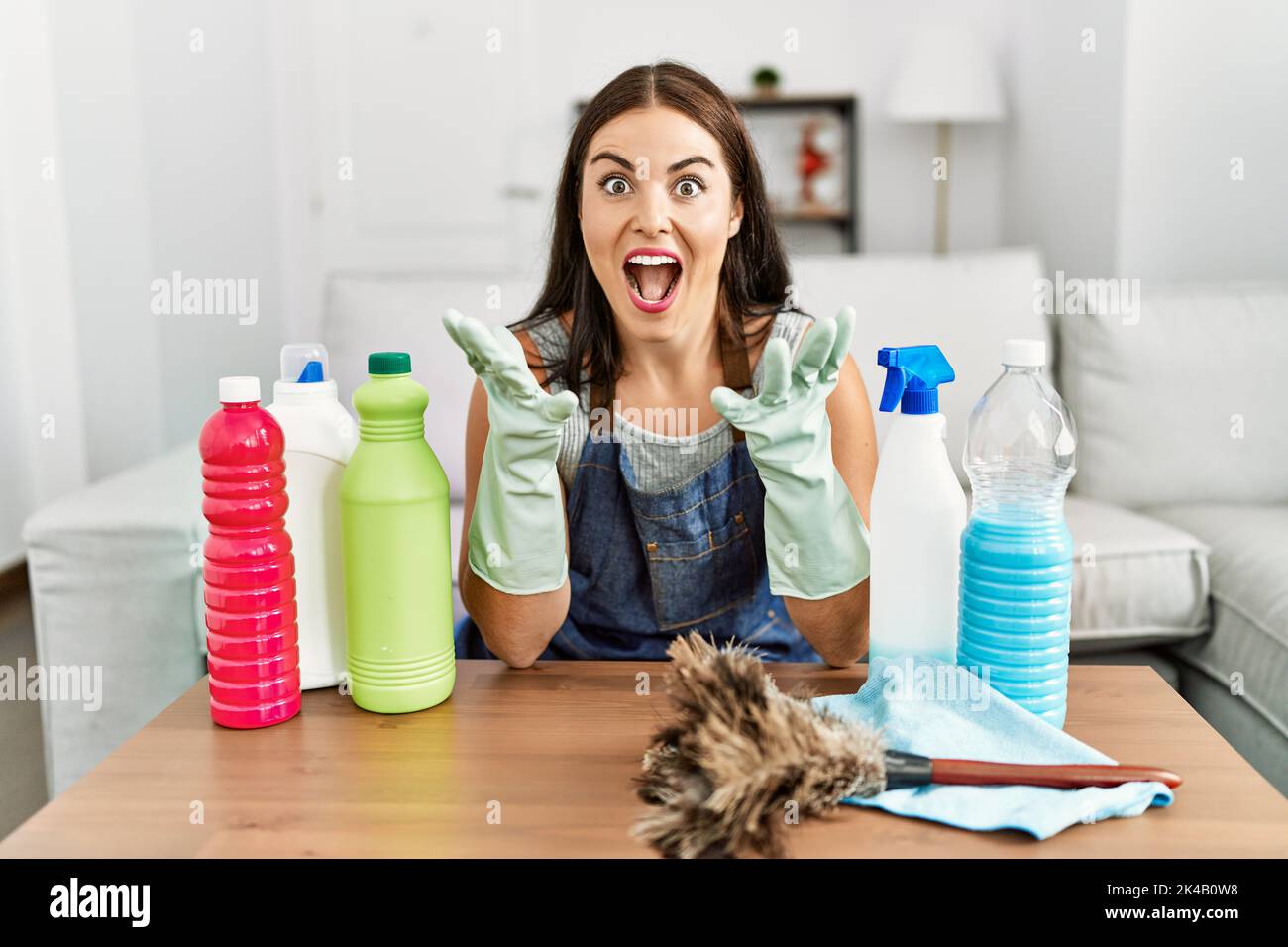 Young brunette woman wearing cleaner apron and gloves cleaning at home ...