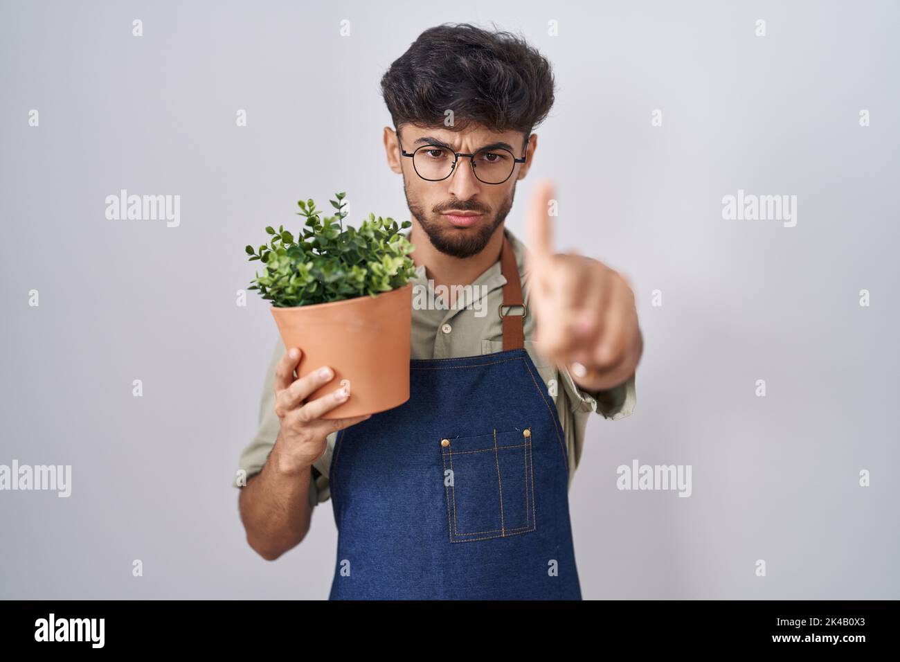 Arab man with beard holding green plant pot pointing with finger up and ...