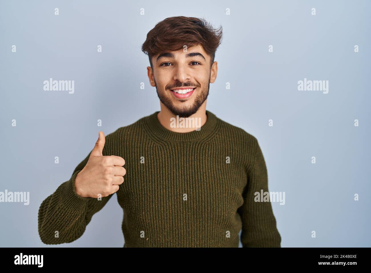 Arab man with beard standing over blue background doing happy thumbs up ...