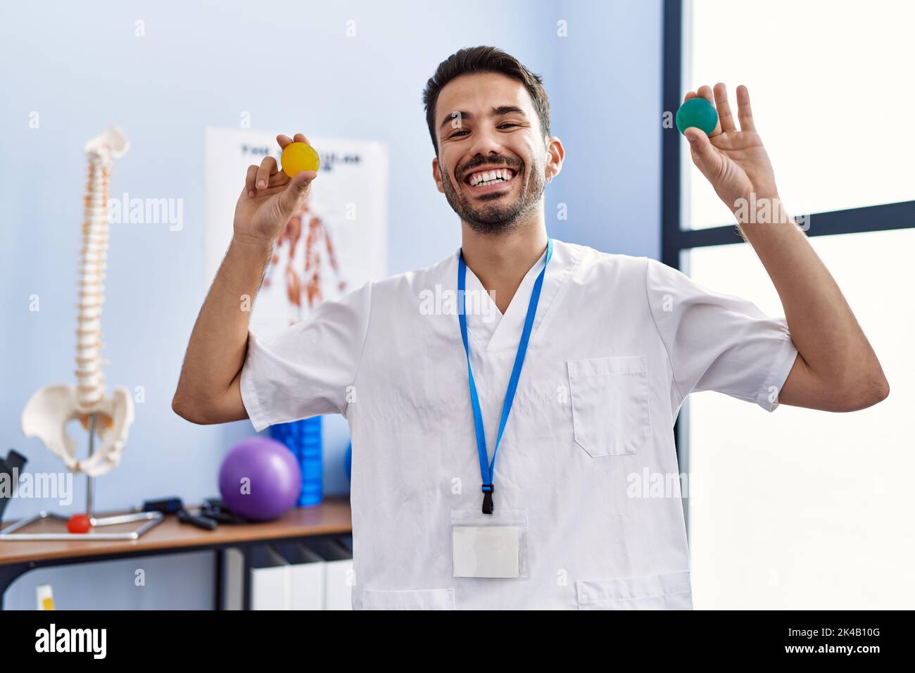 Young hispanic physiotherapist man holding strength balls to train hand ...