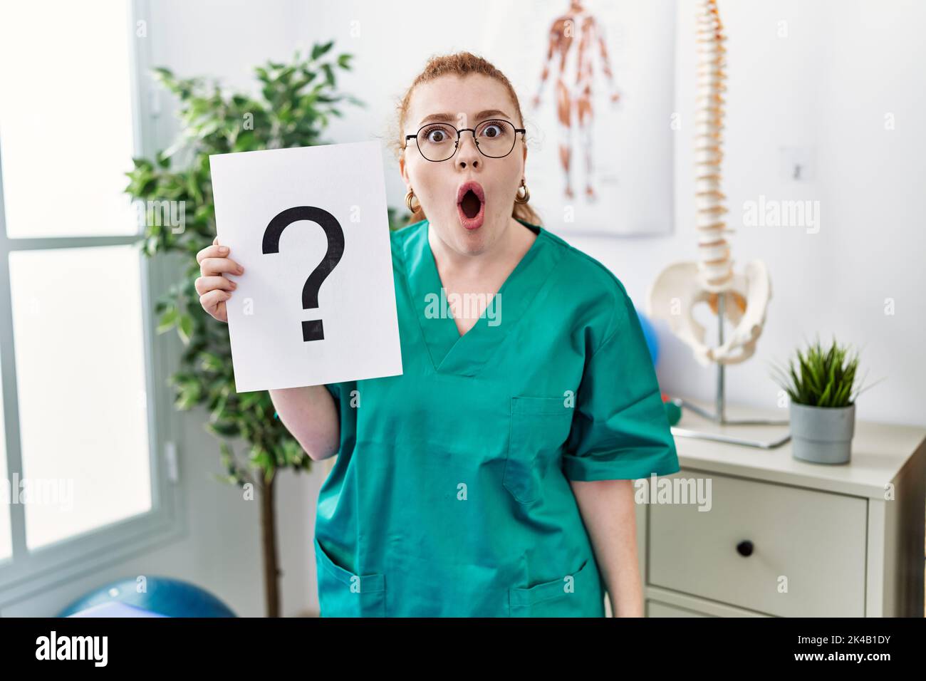 Young redhead physiotherapist woman holding question mark at the clinic ...