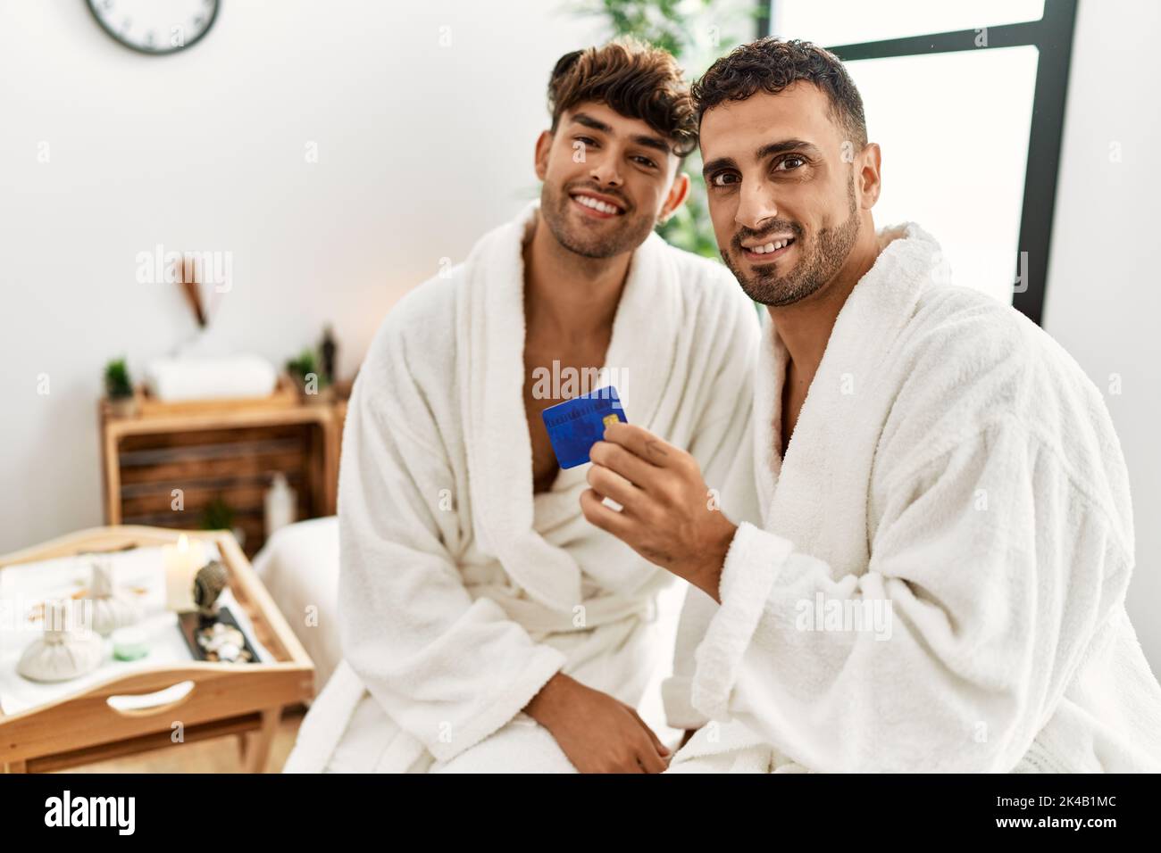 Two hispanic men couple holding credit card sitting on massage table at ...