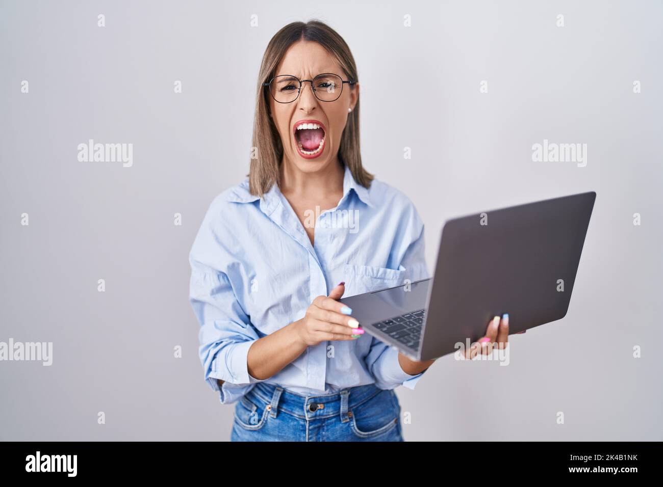 Young woman working using computer laptop angry and mad screaming ...