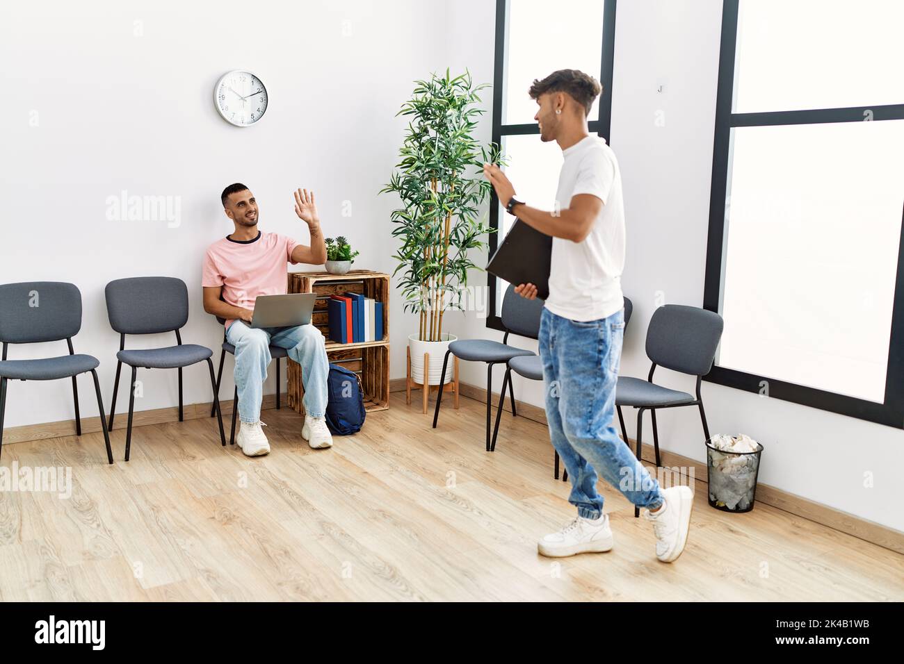 Two hispanic men using laptop saying bye at waiting room Stock Photo ...