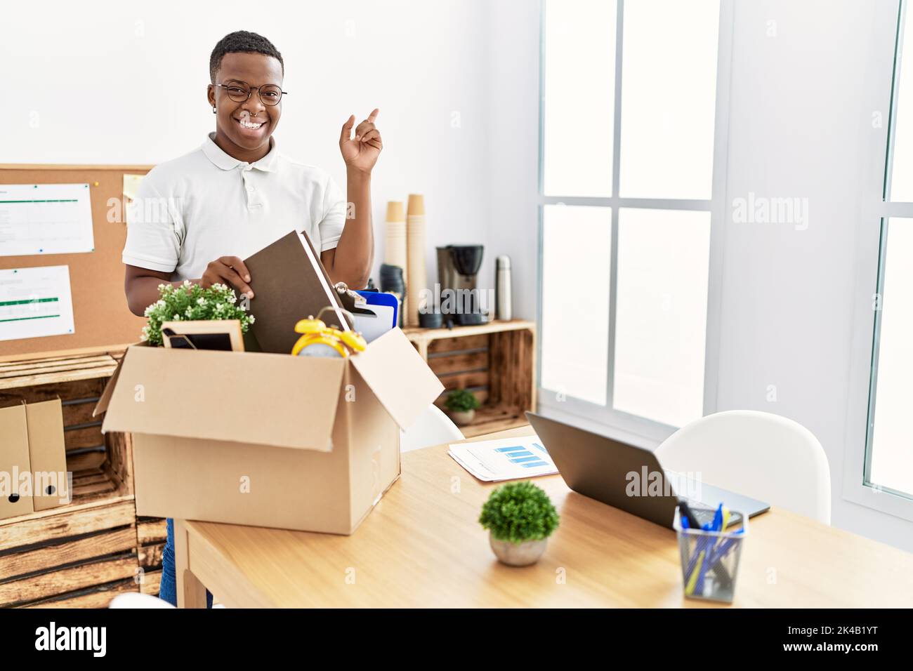 Young african man putting office objects into cardboard box smiling ...