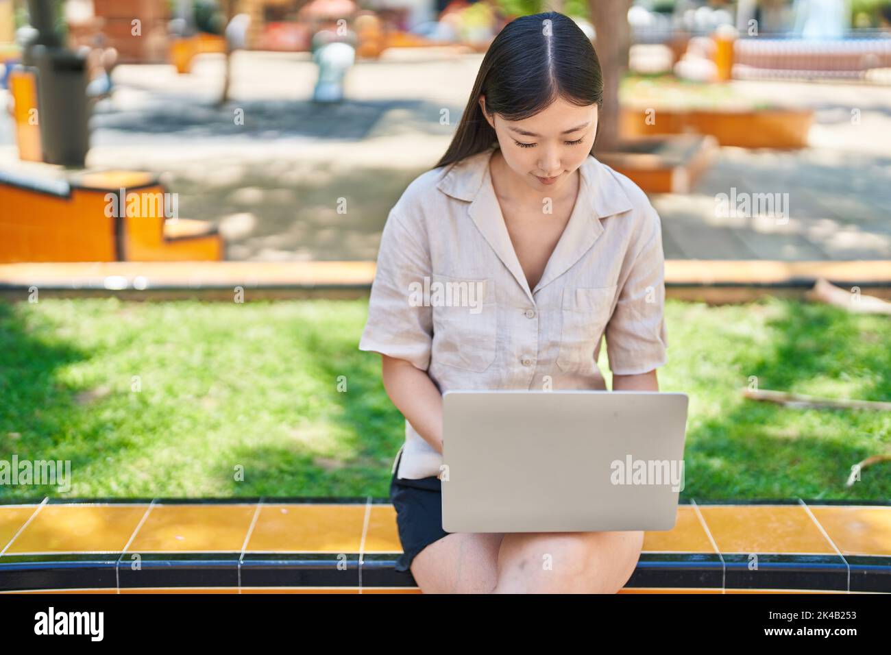 Chinese woman using laptop sitting on bench at park Stock Photo - Alamy