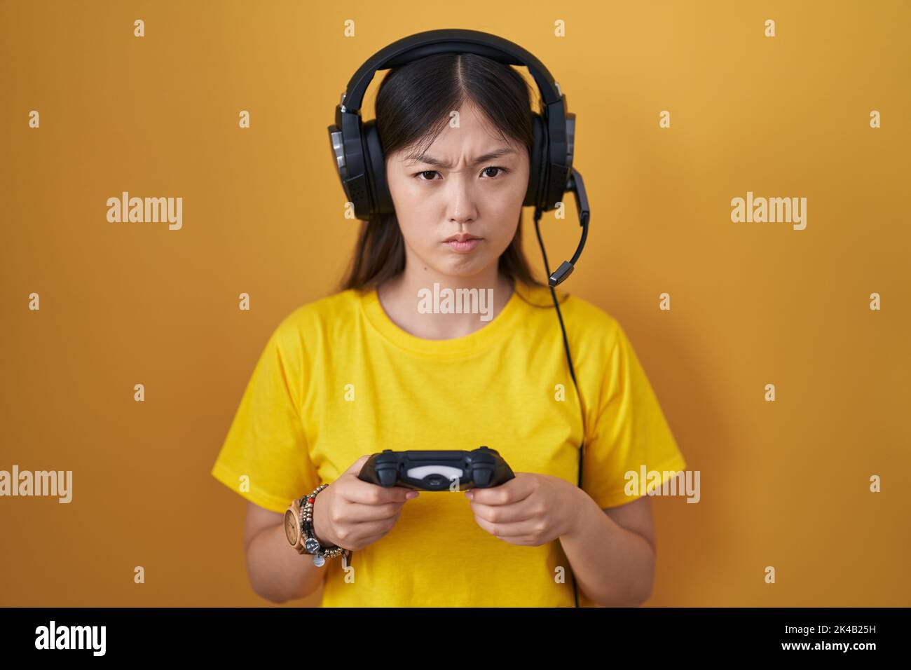 Chinese young woman playing video game holding controller skeptic and ...