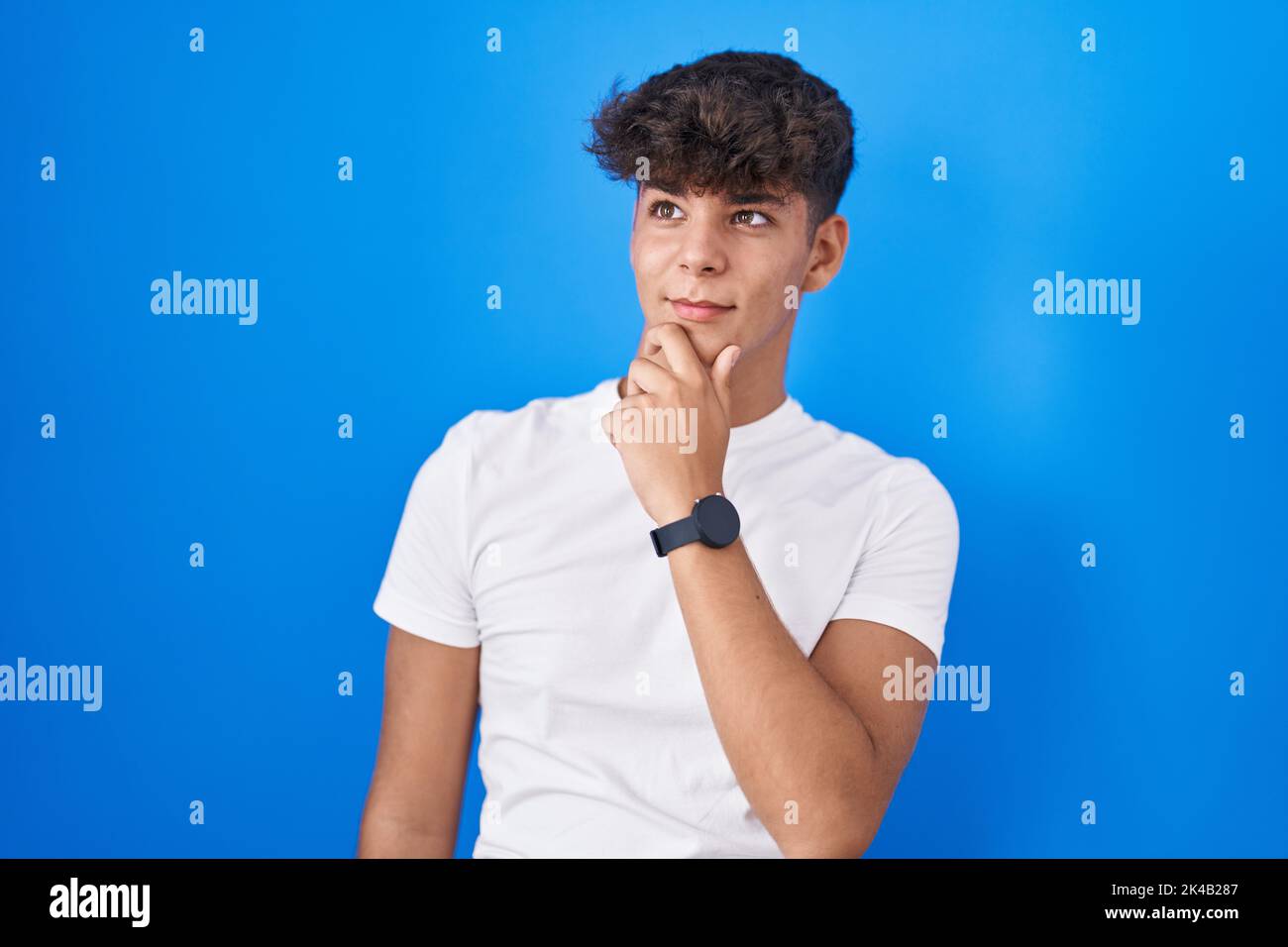 Hispanic teenager standing over blue background thinking worried about ...