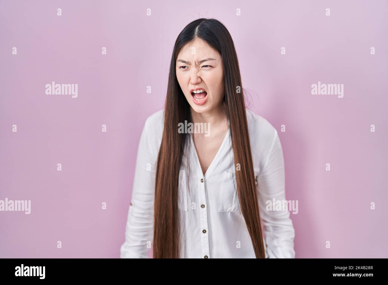 Chinese young woman standing over pink background angry and mad ...