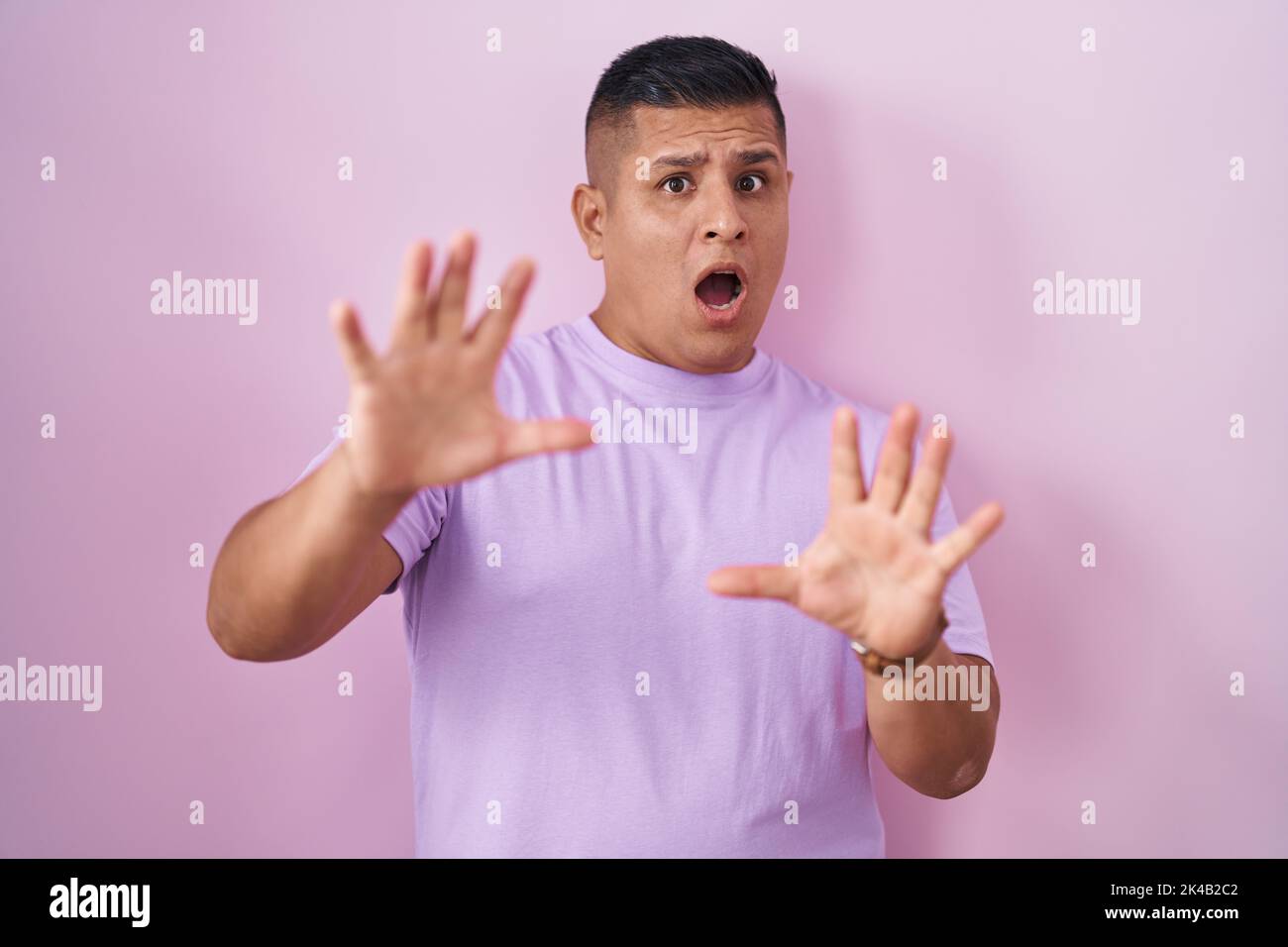 Young hispanic man standing over pink background afraid and terrified ...