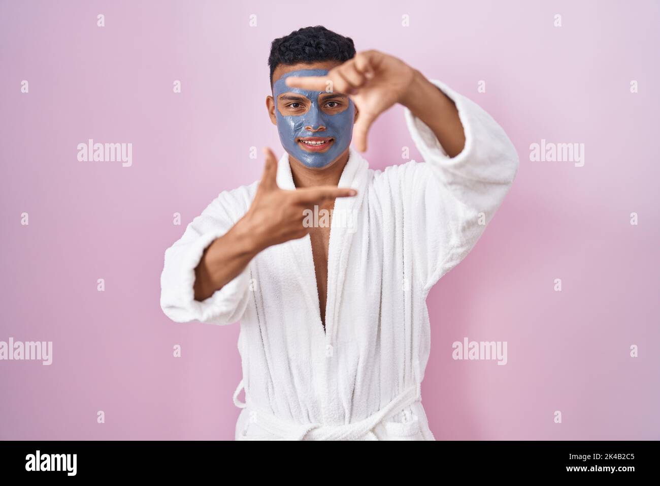 Young hispanic man wearing beauty face mask and bath robe smiling ...