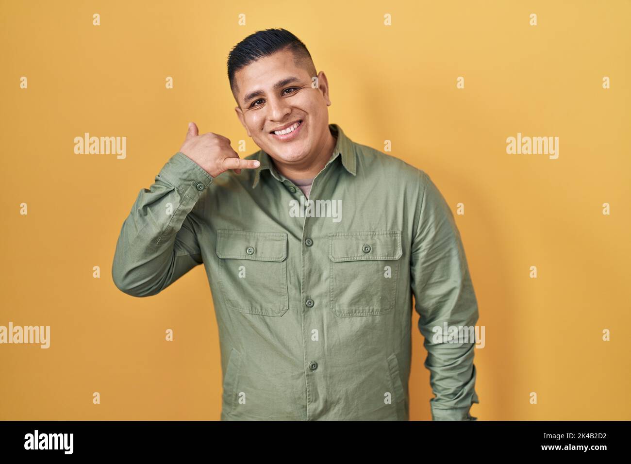 Hispanic young man standing over yellow background smiling doing phone ...