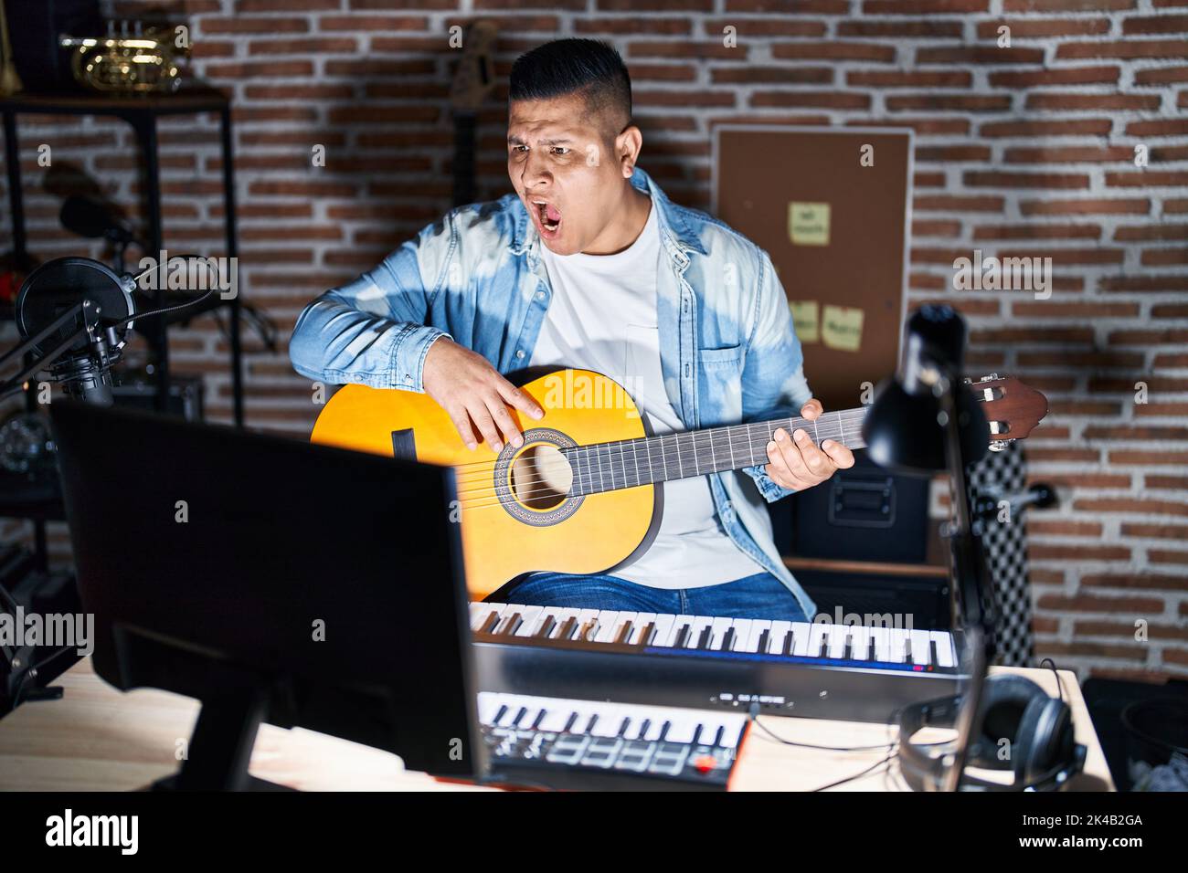 Hispanic young man playing classic guitar at music studio angry and mad ...