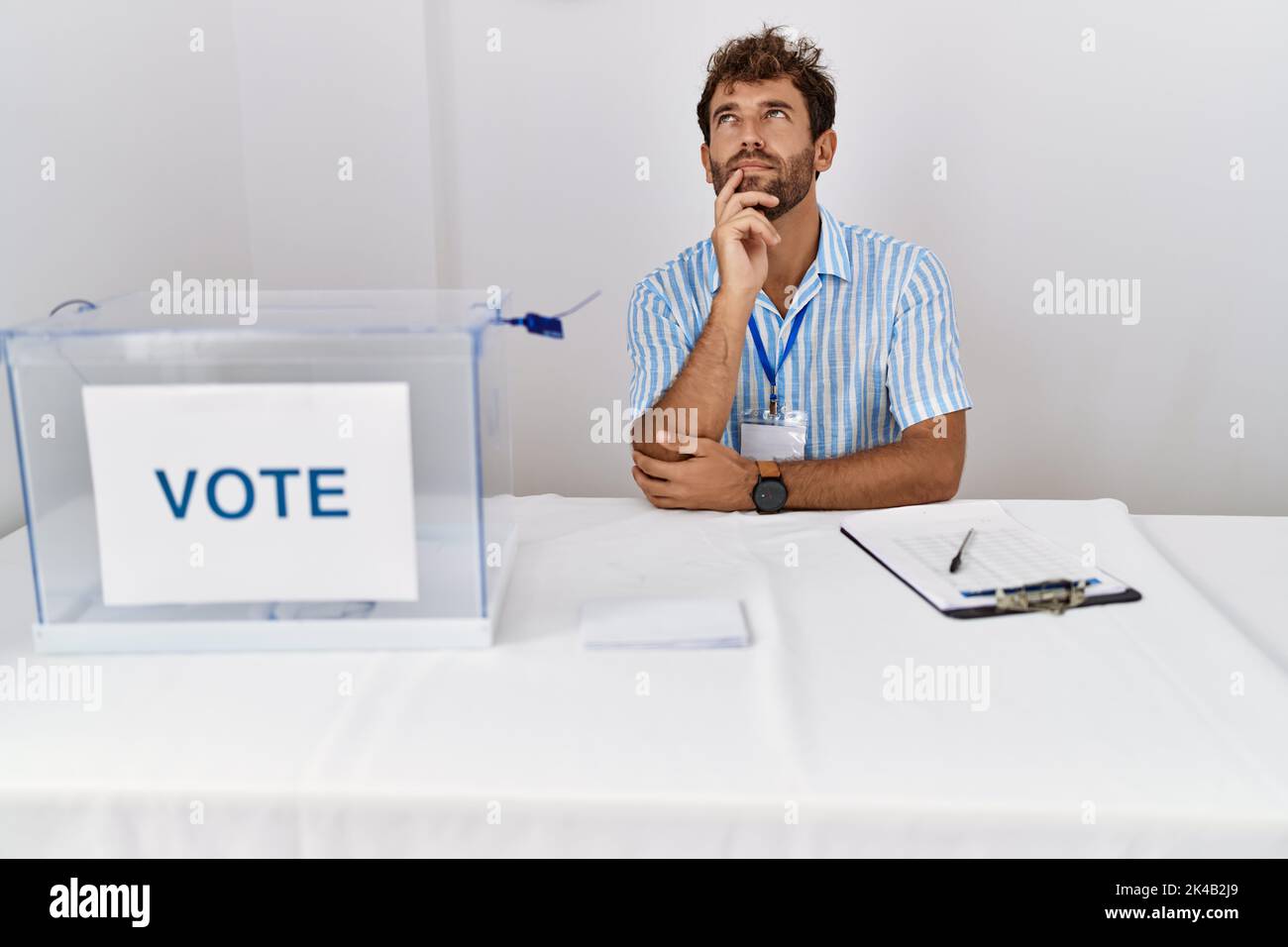 Young handsome man at political election sitting by ballot with hand on ...