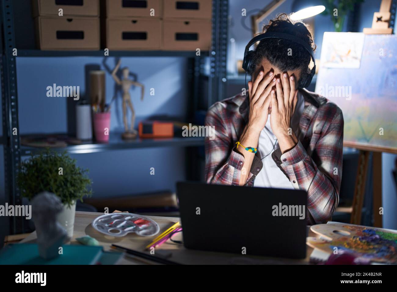 Young hispanic man sitting at art studio with laptop late at night with ...