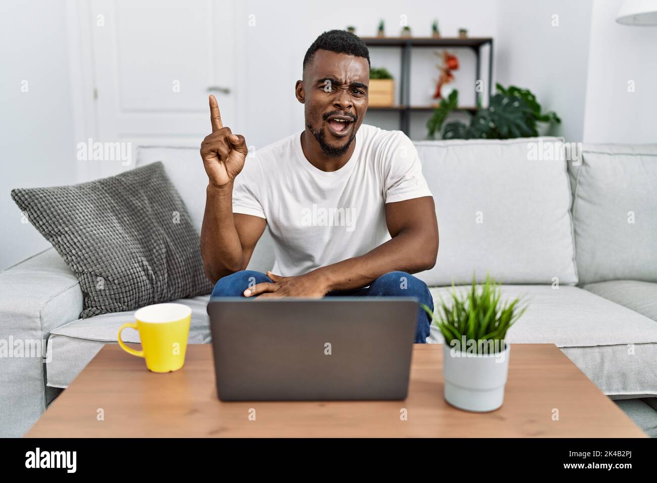 Young african man using laptop at home pointing finger up with ...