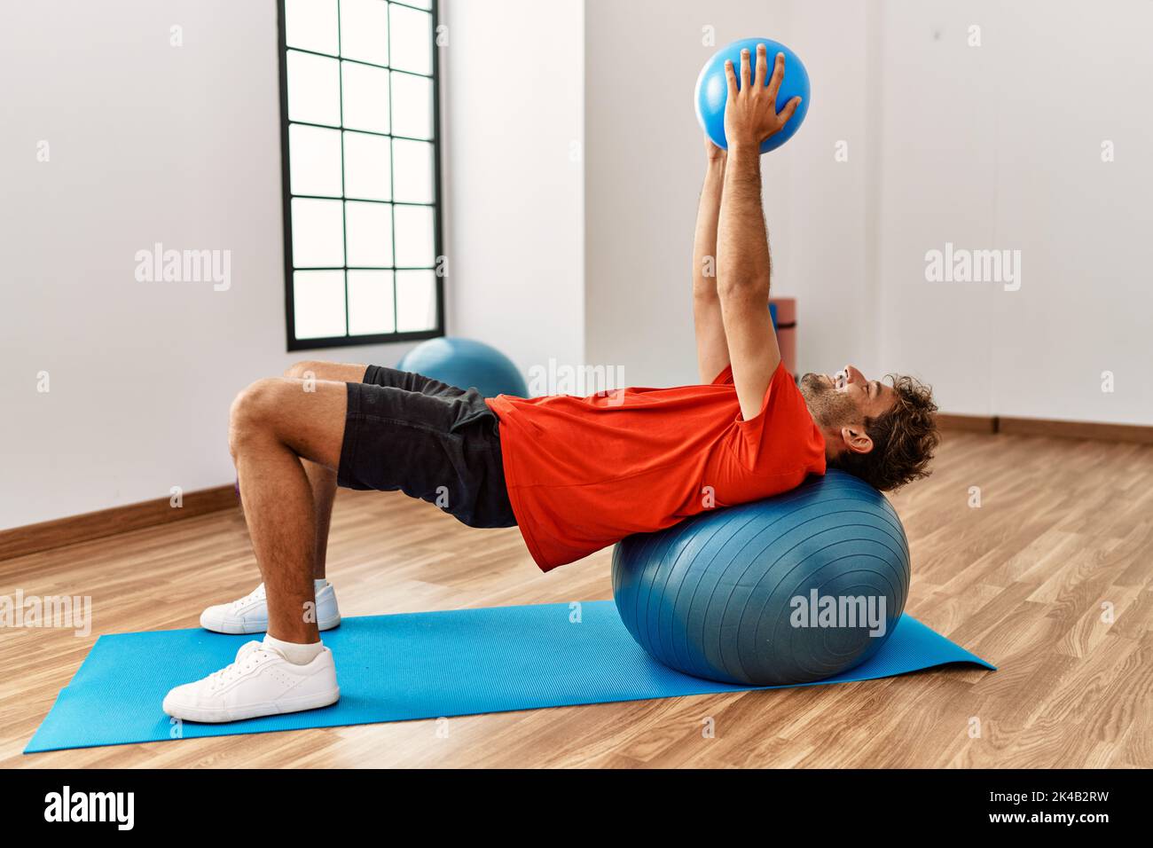 Young hispanic man smiling confident training using fit ball at sport ...