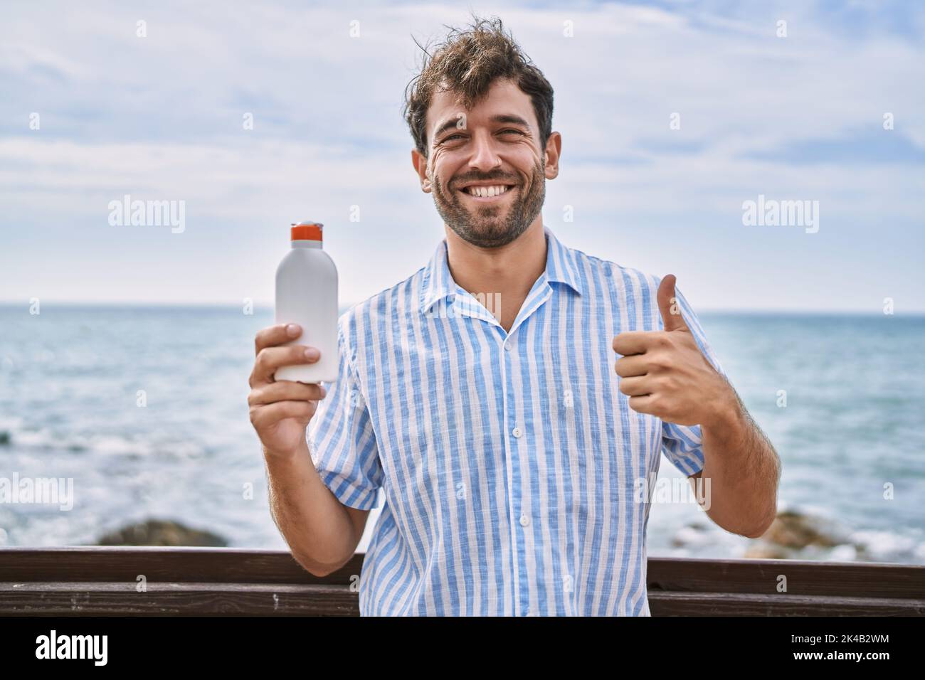Young handsome man holding sunscreen lotion smiling happy and positive ...