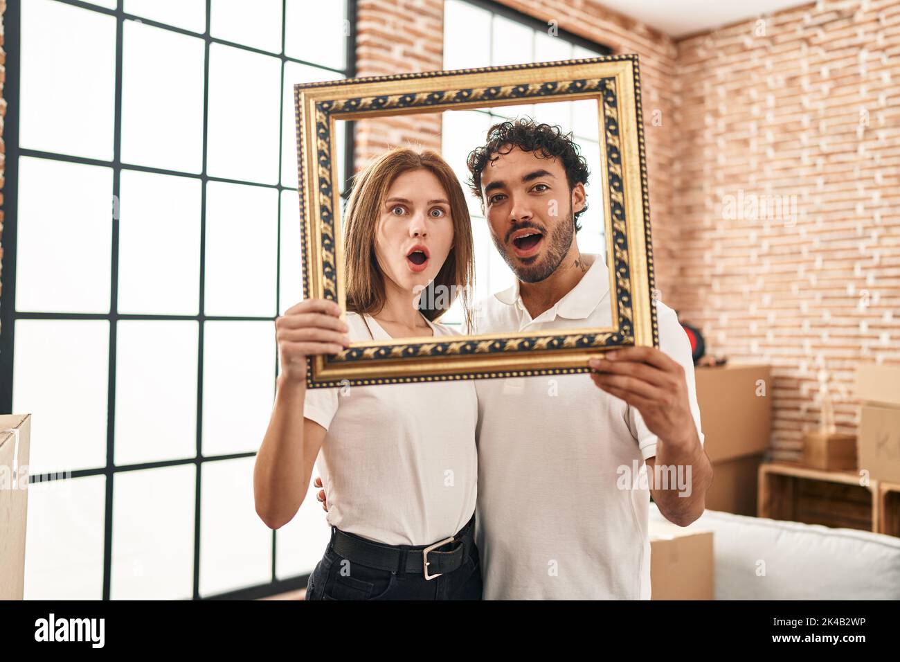 Young two people holding empty frame together afraid and shocked with ...
