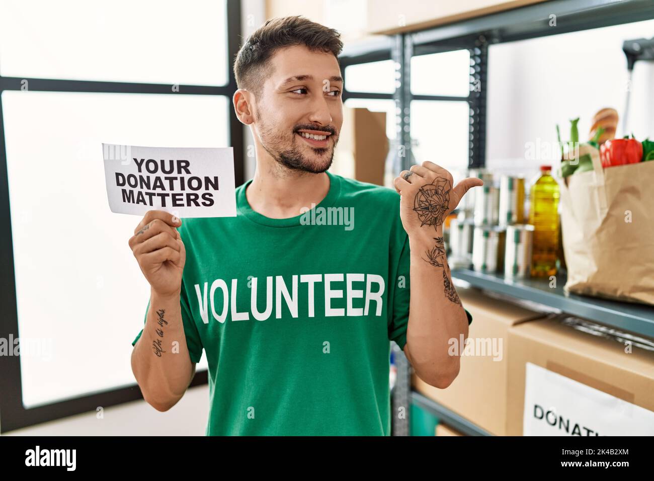 Young volunteer man holding your donation matters banner pointing thumb ...