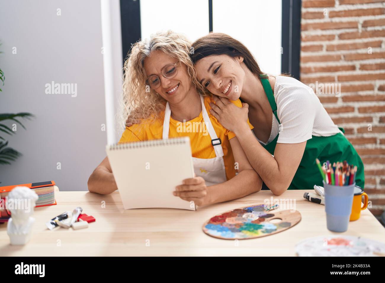 Two women artists smiling confident drawing on notebook at art studio ...