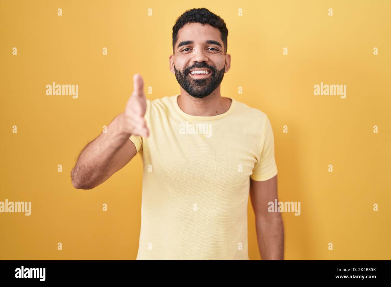 Hispanic man with beard standing over yellow background smiling ...