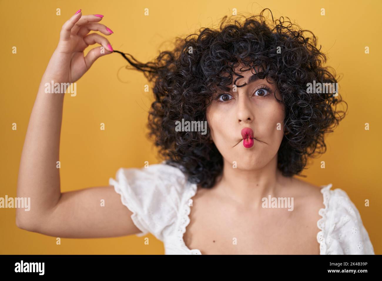 Young brunette woman with curly hair holding curl making fish face with ...