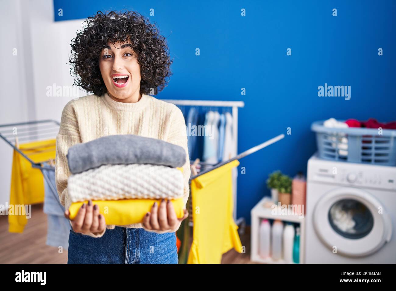 Young brunette woman with curly hair holding clean laundry celebrating crazy and amazed for ...