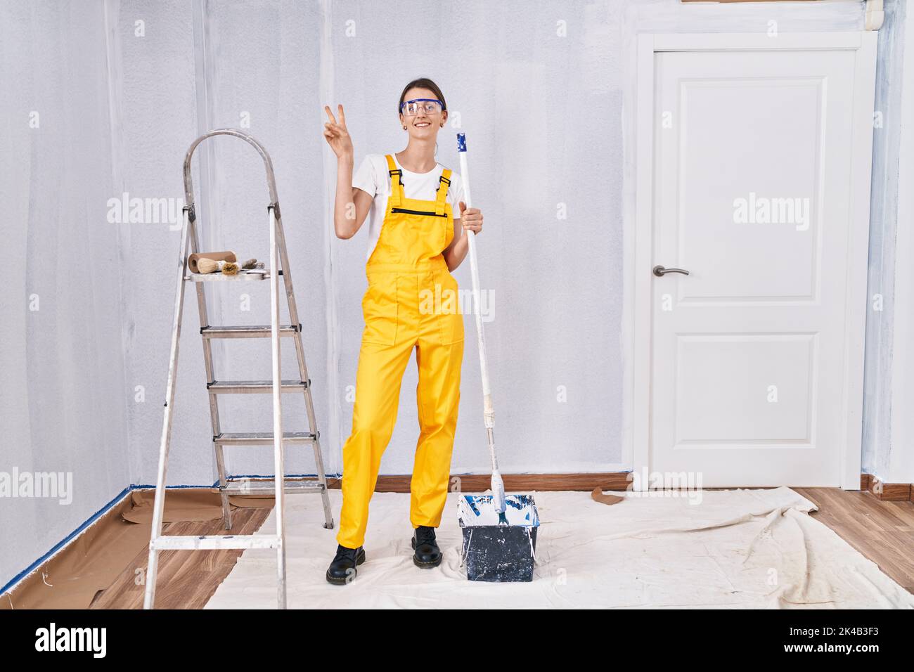 Young caucasian woman painting walls smiling with happy face winking at ...