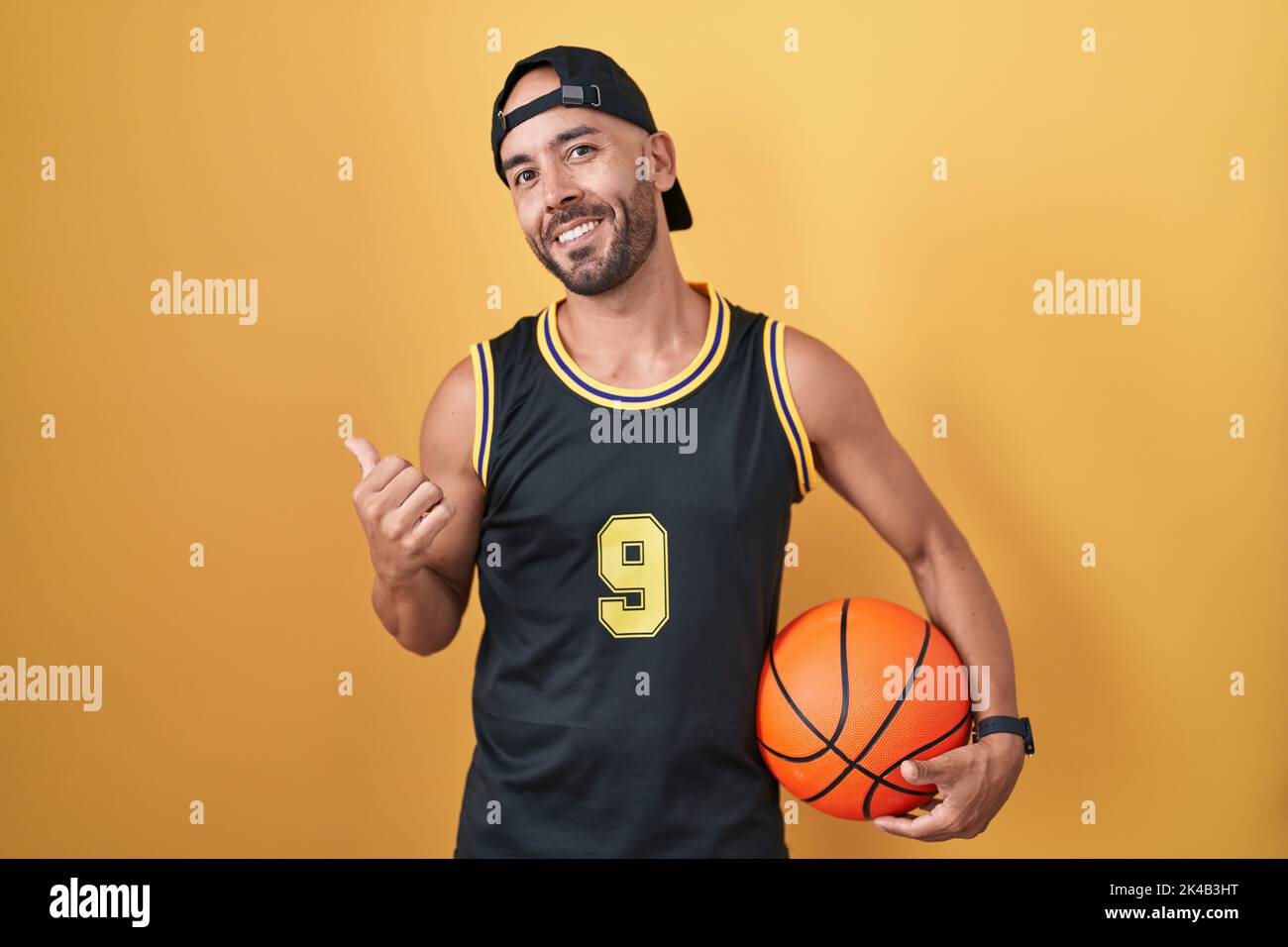 Middle age bald man holding basketball ball over yellow background ...
