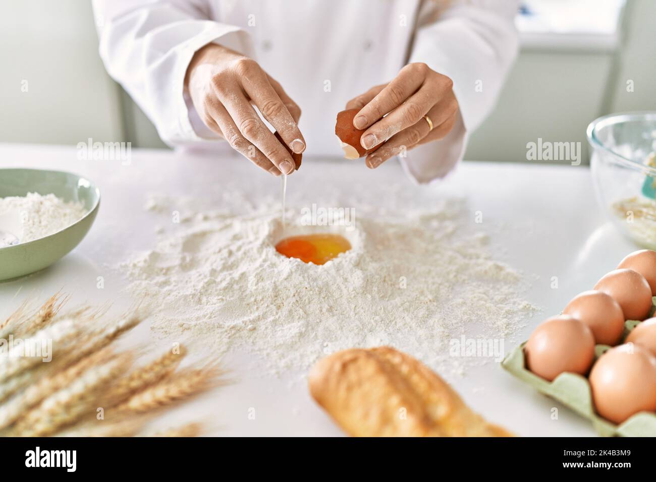 Young woman wearing cook uniform cracking egg on flour at kitchen Stock ...