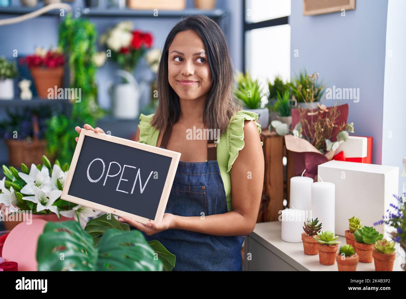 Hispanic young woman working at florist with open sign smiling looking ...