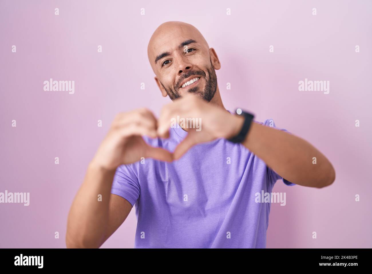 Middle age bald man standing over pink background smiling in love ...