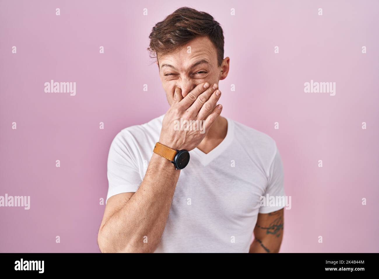Caucasian man standing over pink background smelling something stinky ...