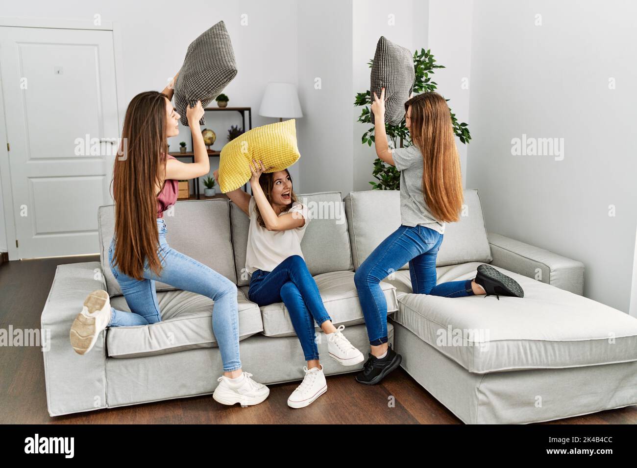 Three young hispanic woman smiling happy fighting with pillowa at home ...