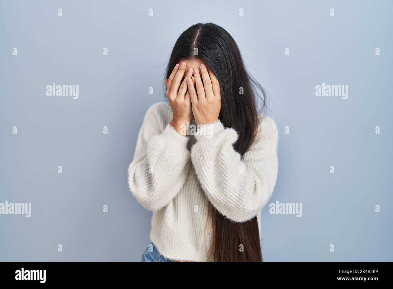 Young hispanic woman wearing casual sweater over blue background with ...