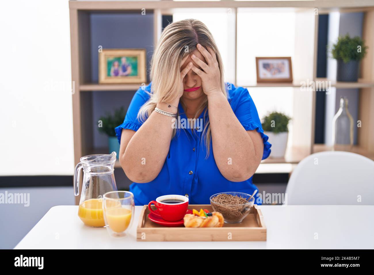 Caucasian plus size woman eating breakfast at home with sad expression ...