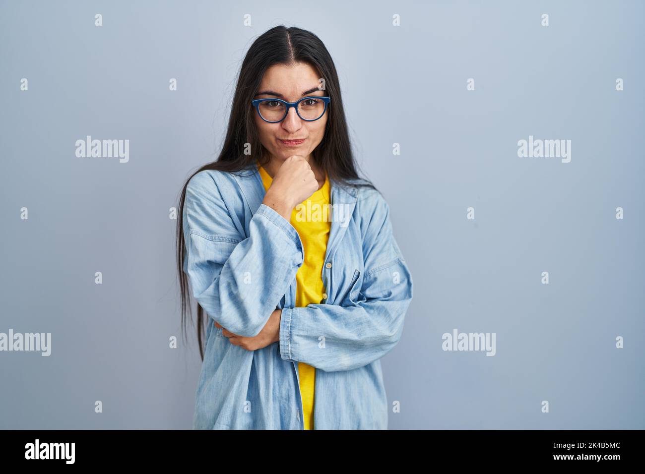 Young hispanic woman standing over blue background looking confident at ...