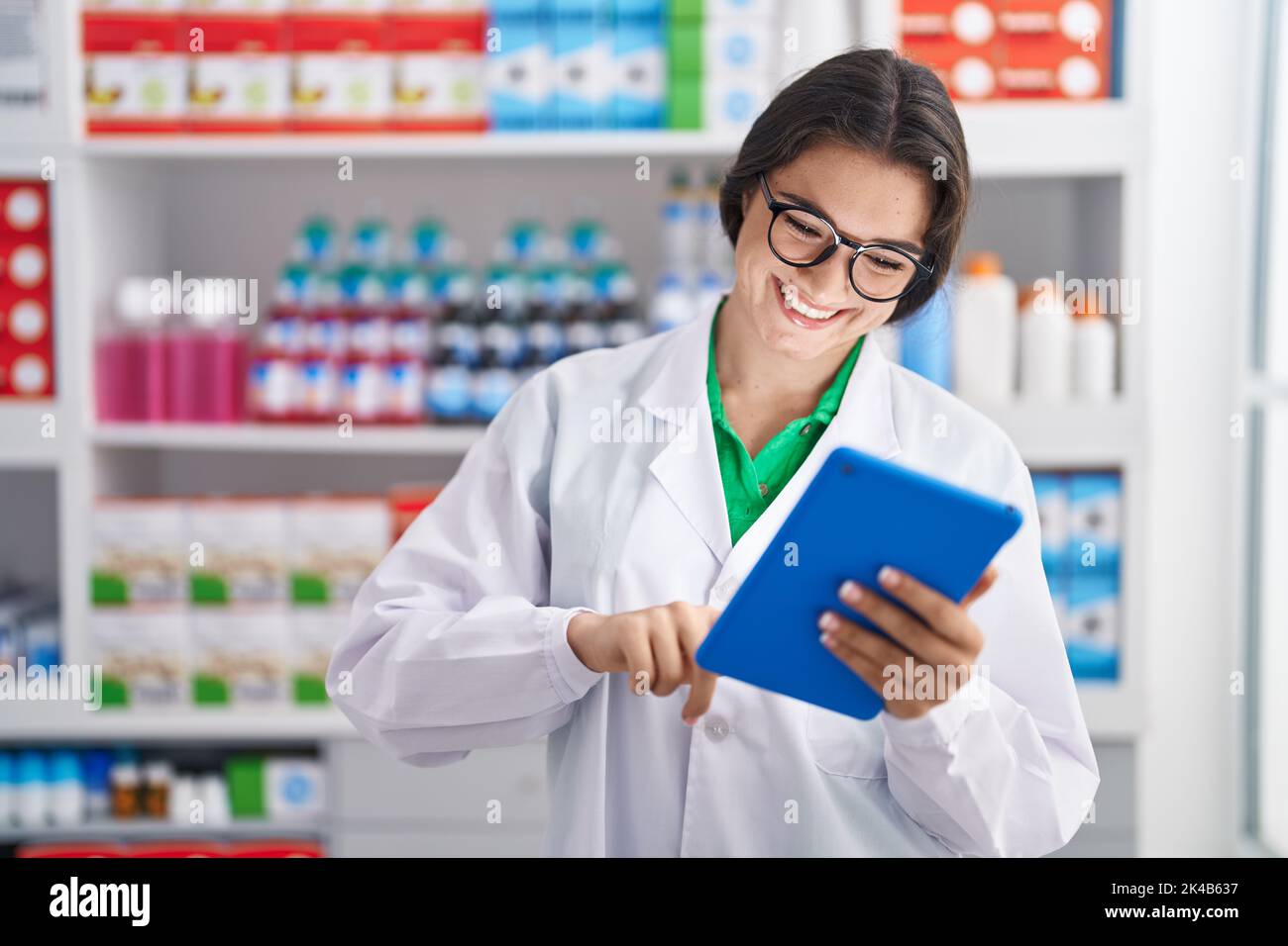 Young hispanic woman pharmacist smiling confident using touchpad at ...