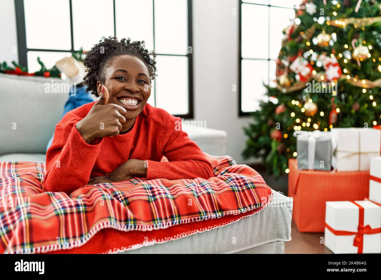 Young african american woman lying on the sofa by christmas tree doing ...