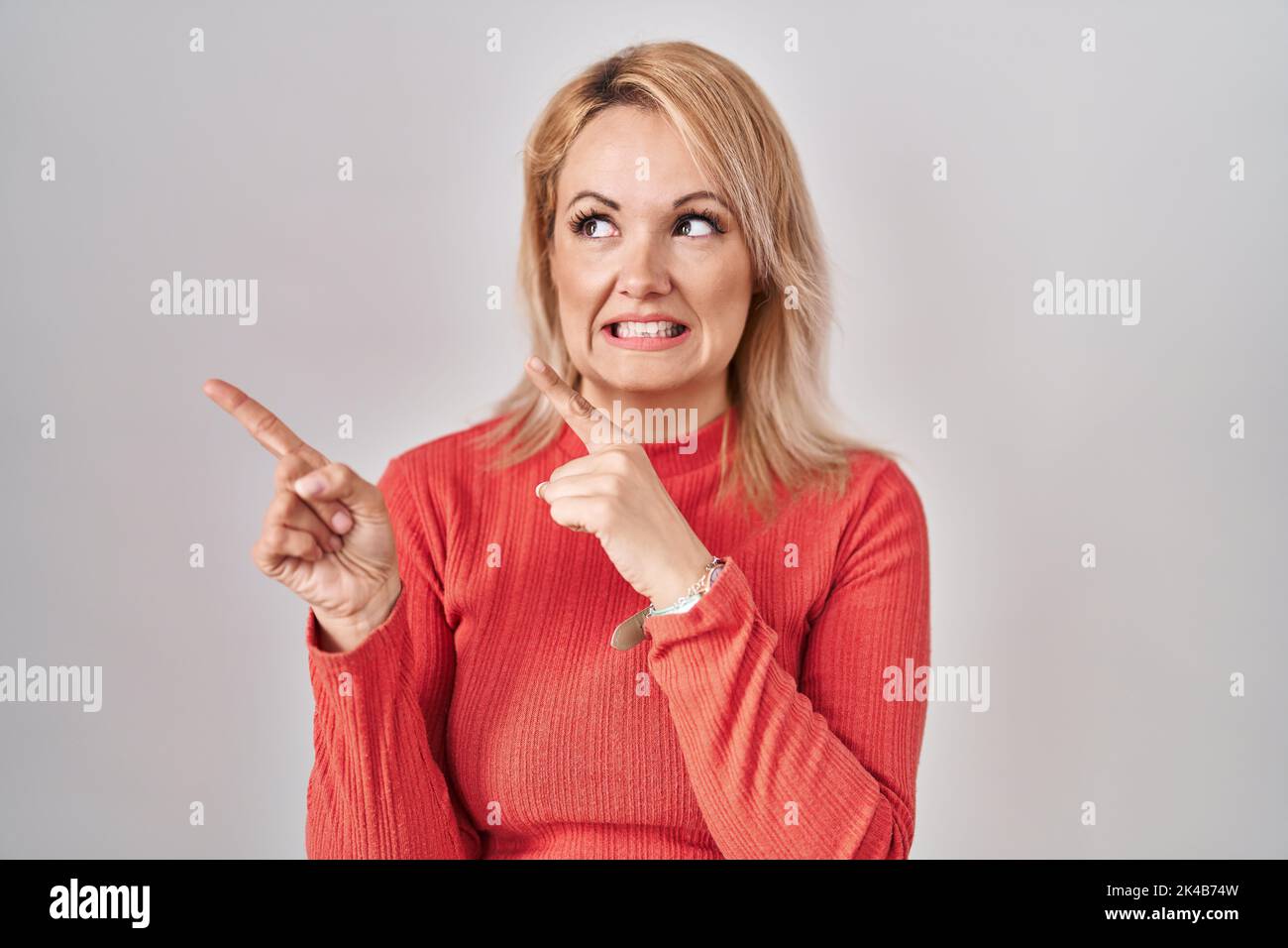 Blonde woman standing over isolated background pointing aside worried ...