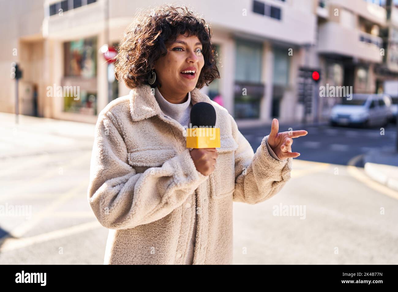 Young beautiful hispanic woman reporter working using microphone at ...